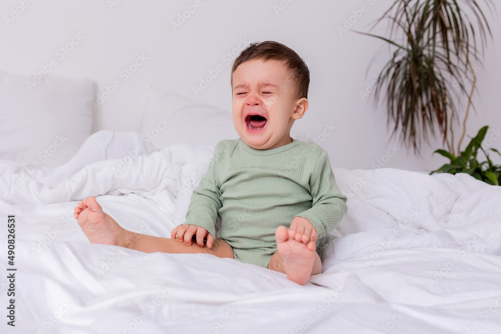 crying baby in a green cotton bodysuit and bare feet is sitting on a ...