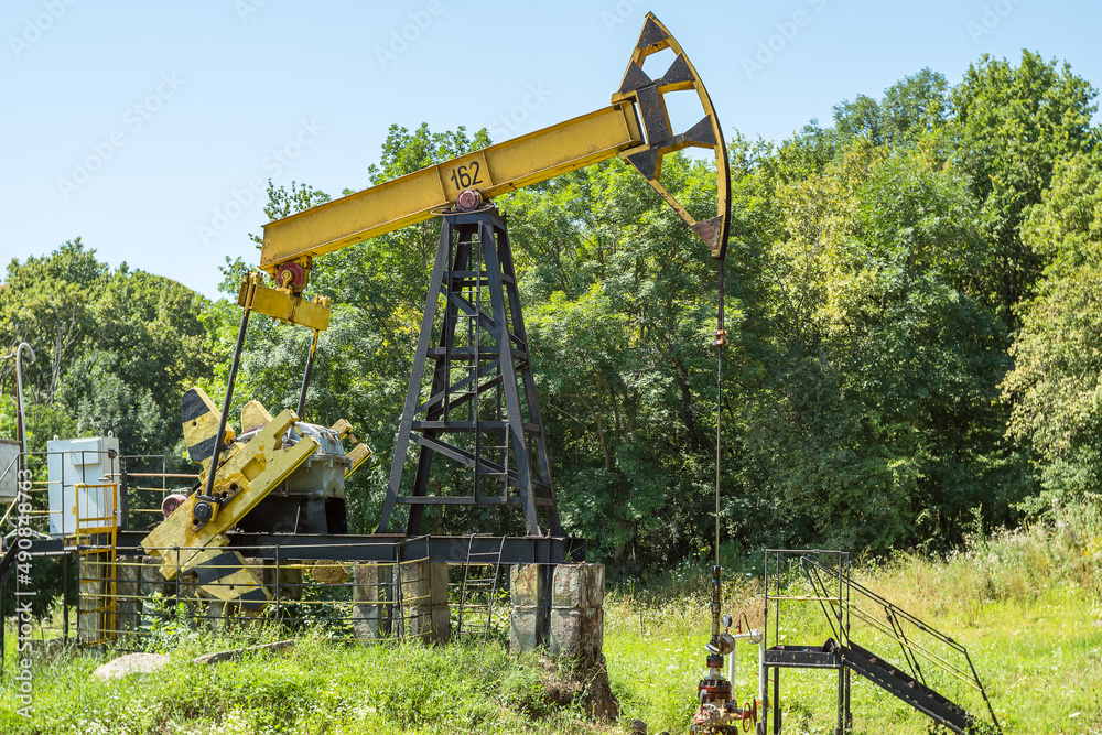An old yellow oil rig pumping oil in a clearing in the woods. In the ...