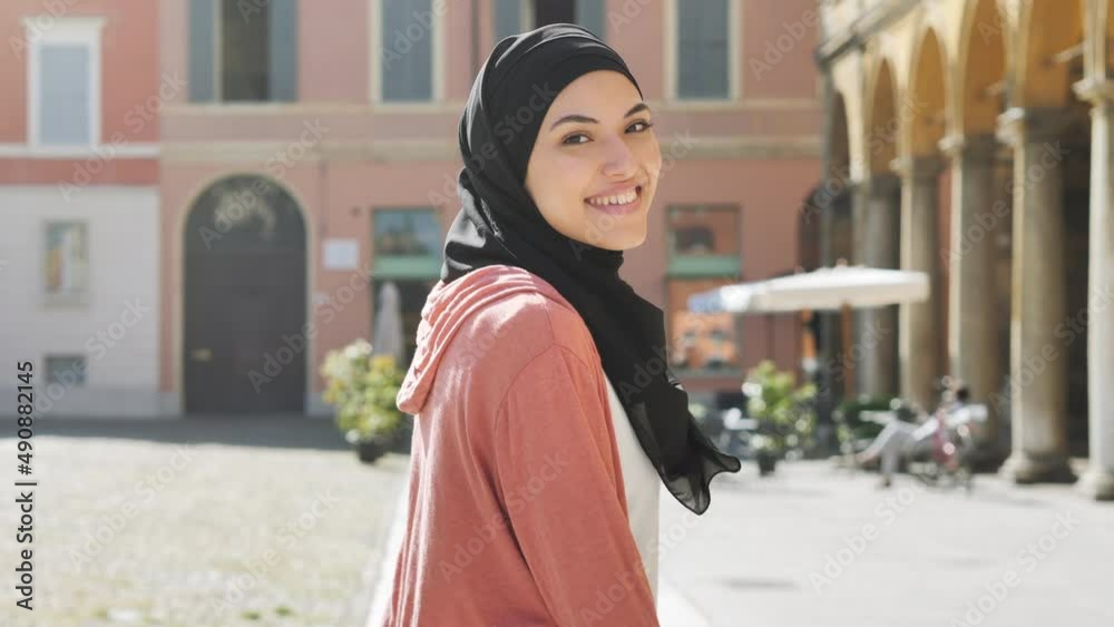 muslim girl walking in city center turns around and smile to the camera ...