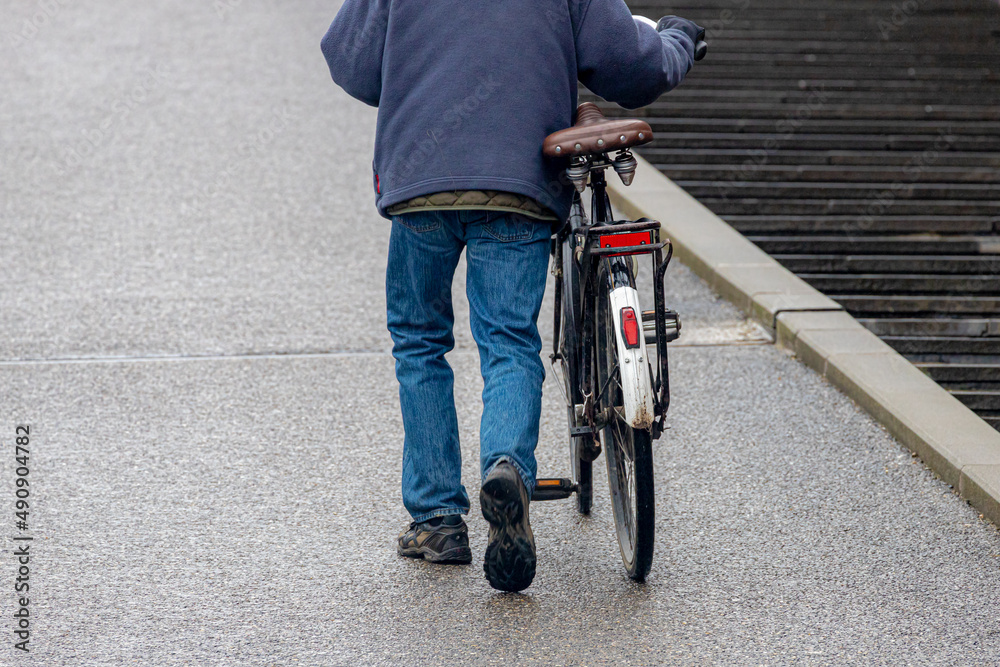 Back view of a Dutch man carrying classic vintage bike up to slope ...