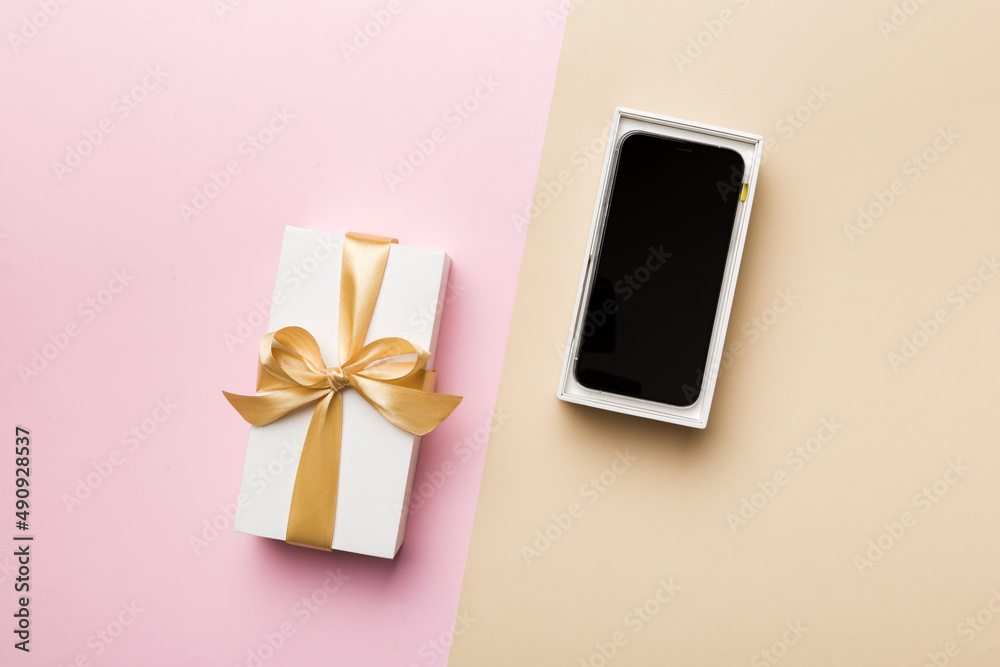 Opened gift box with gold ribbon and smartphone on color background ...