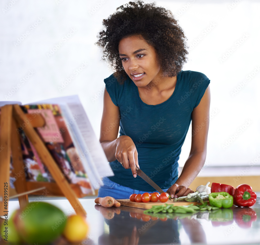 Am I doing this correctly. A young woman cooking from a recipe book ...