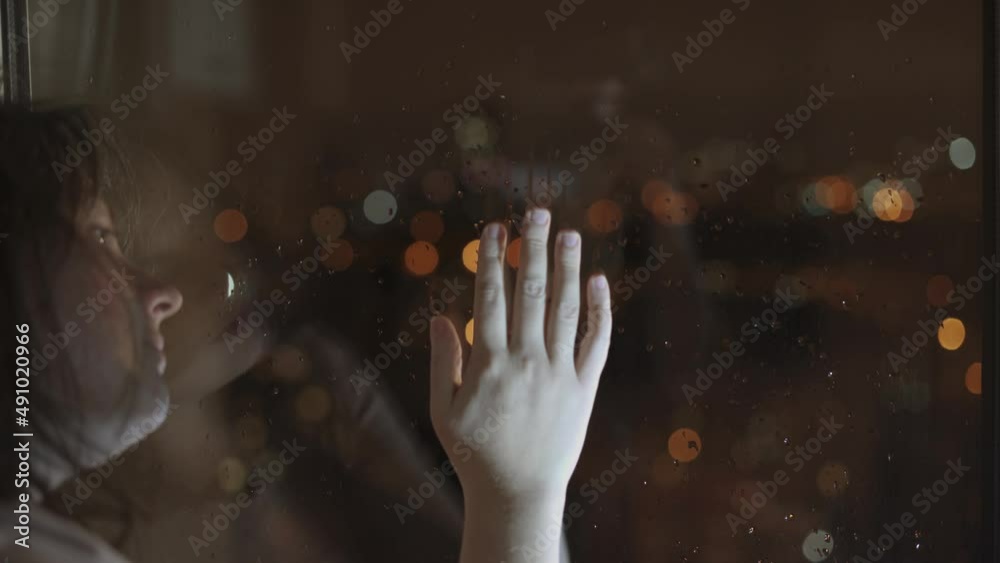 Sad young woman leans face against window with raindrops. Depressed ...