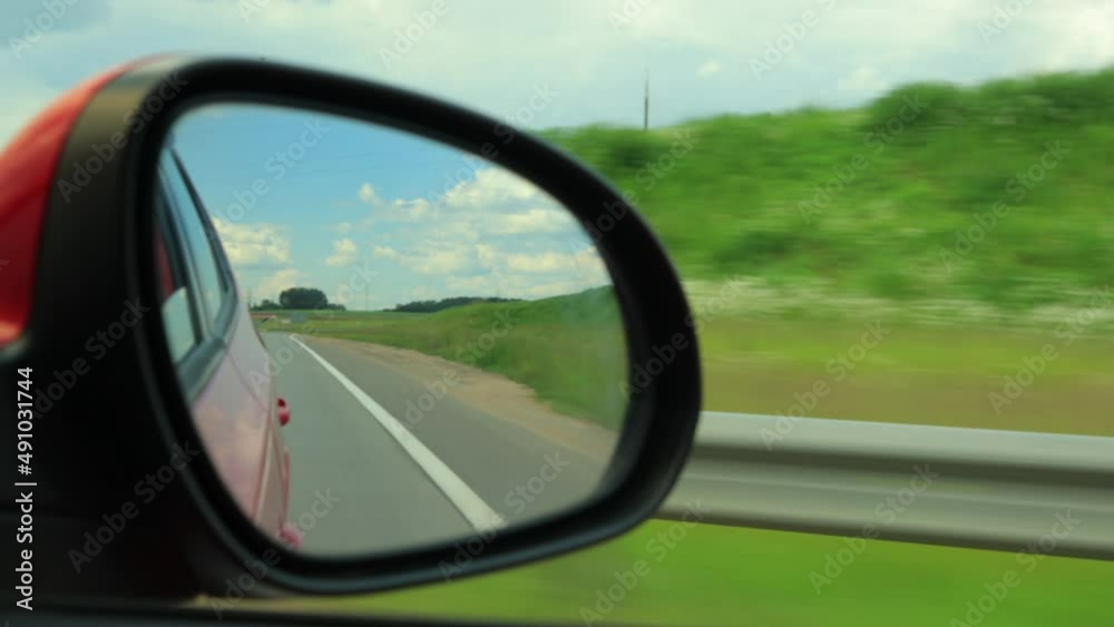 View in the side rear view mirror of a car driving a red car on a ...