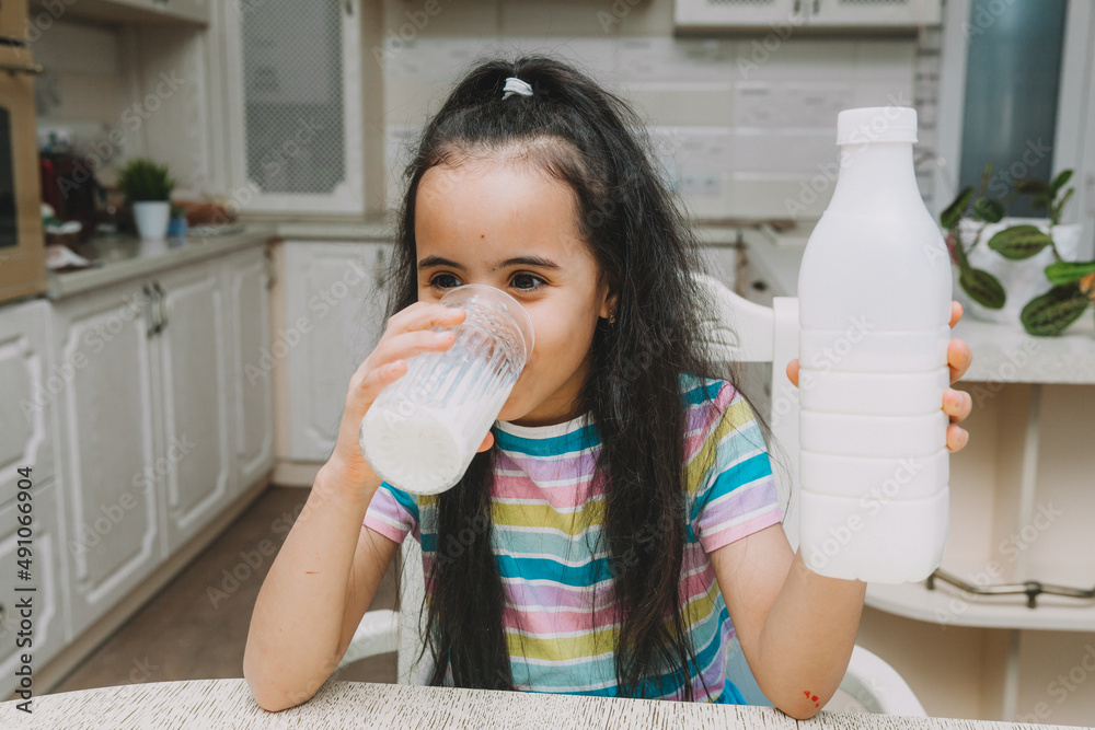 Cute little girl drinks milk at the table in the kitchen. the child is ...
