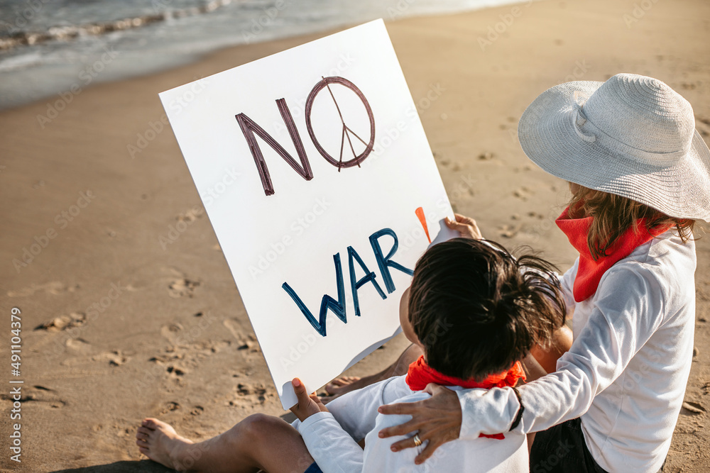 a mother and son sitting on the shore of the beach while reading a sign ...