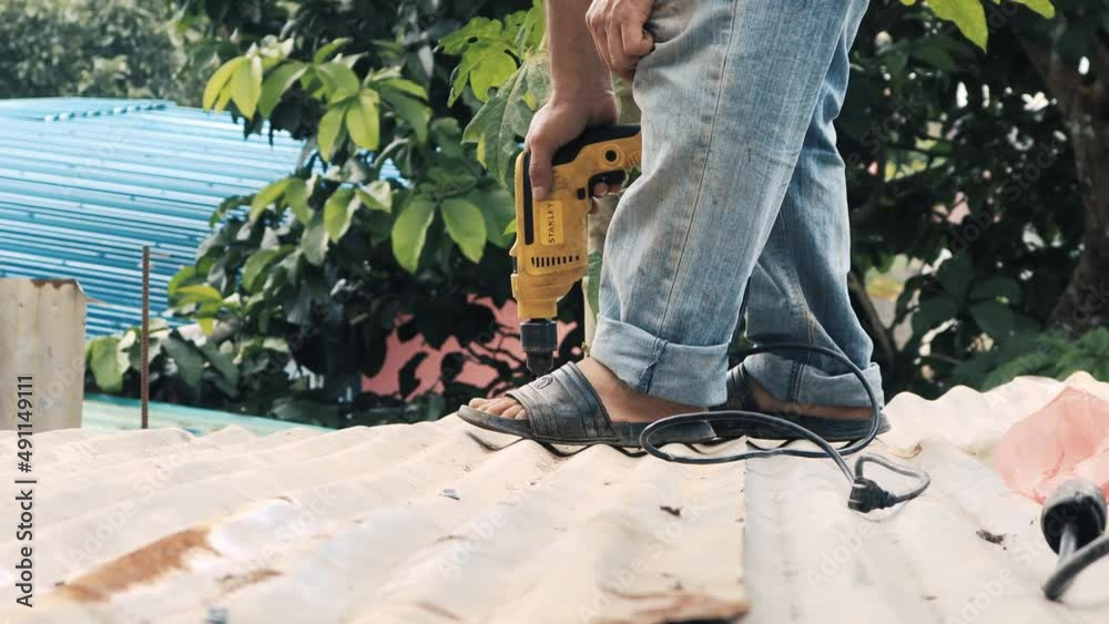 Construction worker on slides drilling a screw on a zinc sheet roof ...
