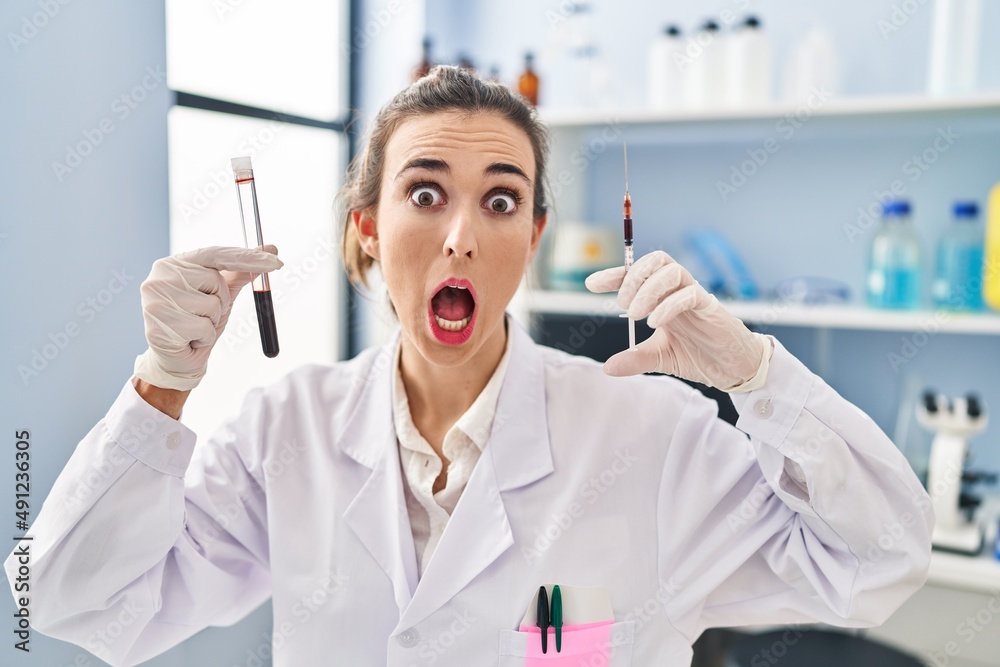 Young woman working at scientist laboratory holding blood sample afraid ...