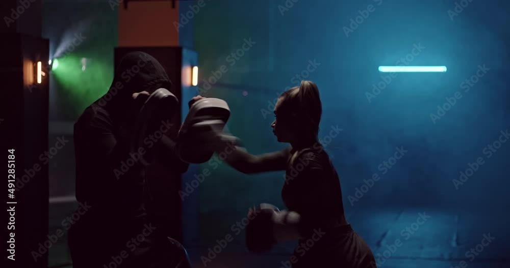 Female boxer trains with a trainer in a dark gym. Professional athlete ...