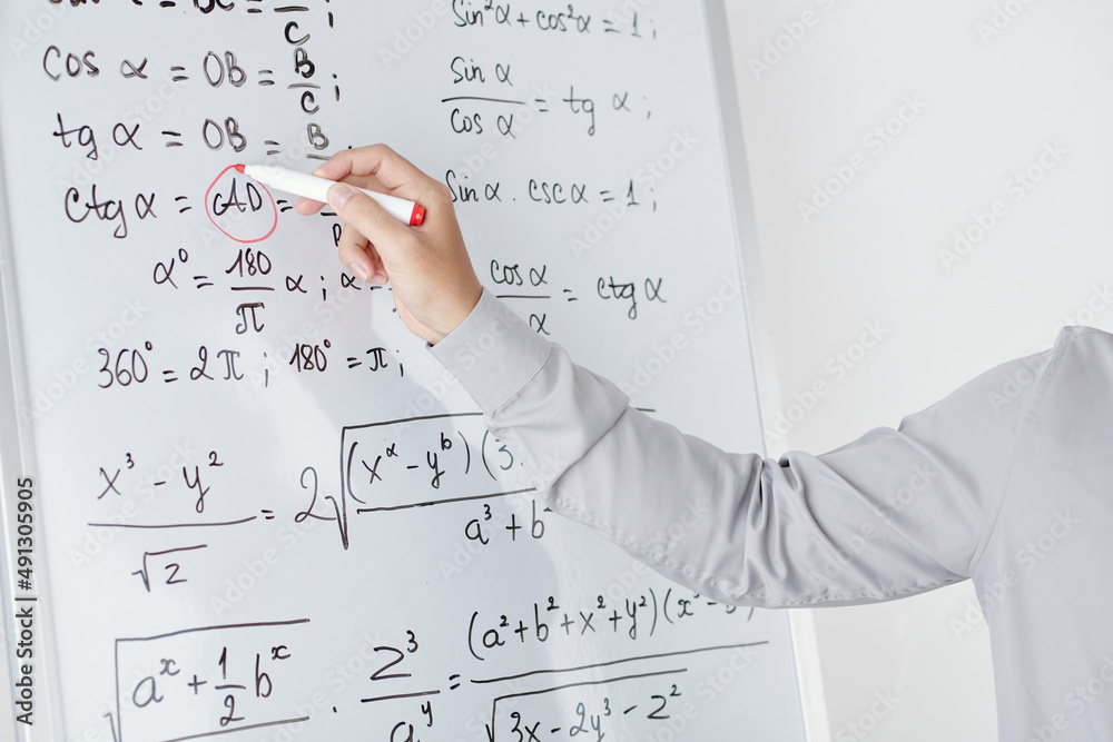 Hands of math teacher circling variable in formula on whiteboard with ...