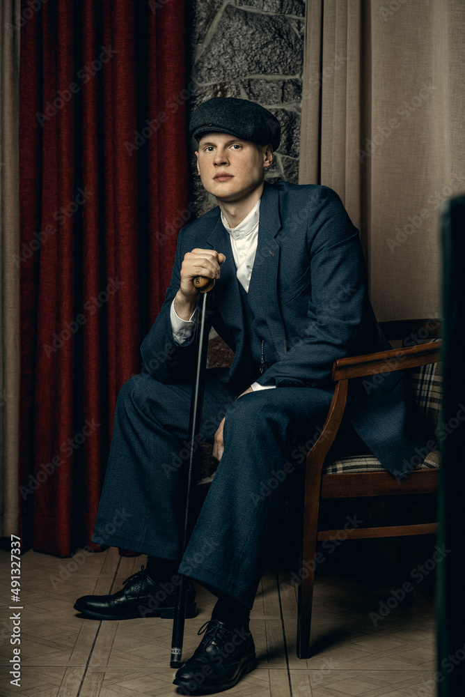 A young man with a cane is sitting in an armchair. English retro ...