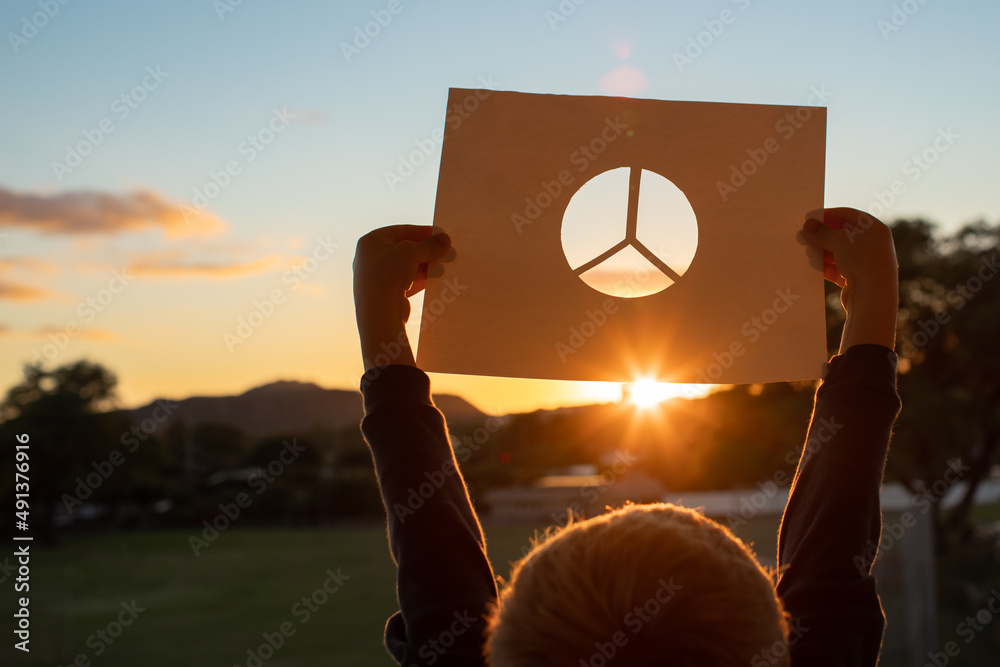 Little child holding up peace symbol against a beautiful sunset. No war ...