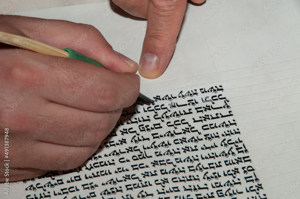 Closeup view of the hands of a Jewish scribe writing the Hebrew text of ...