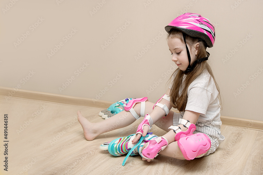 little cute girl in roller skating protection sits on the floor and ...