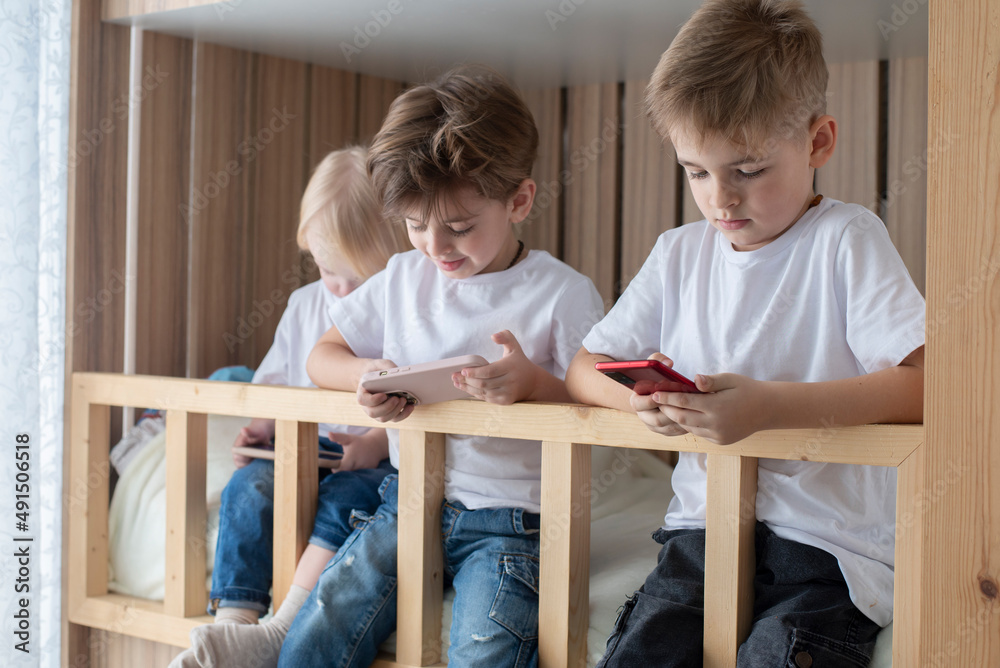 Three different children are sitting on the bed, using wireless gadgets ...
