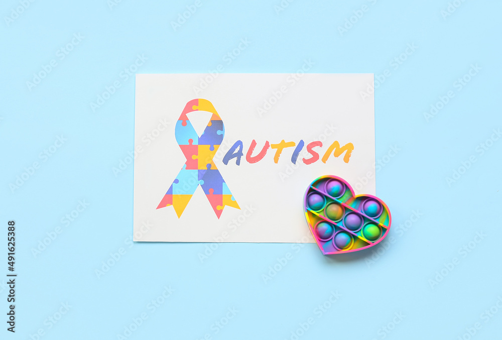Paper sheet with word AUTISM, awareness ribbon and pop it fidget toy on ...