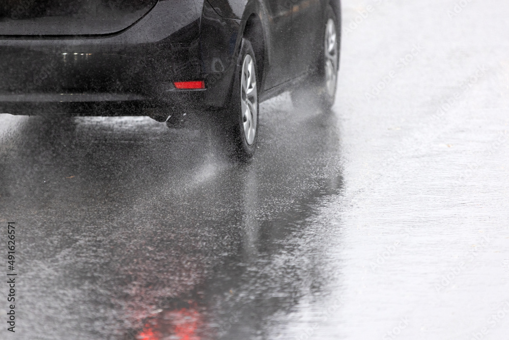 rain water splash flow from wheels of black car moving fast in daylight ...