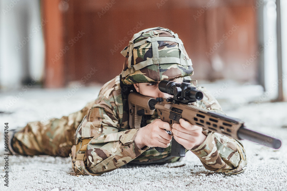 Military soldier in the uniform lay on the ground and holds gun in ...