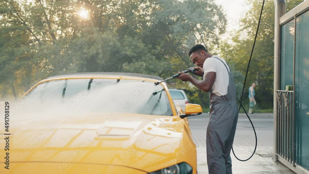 Handsome African guy in t-shirt and protective overalls washing his ...