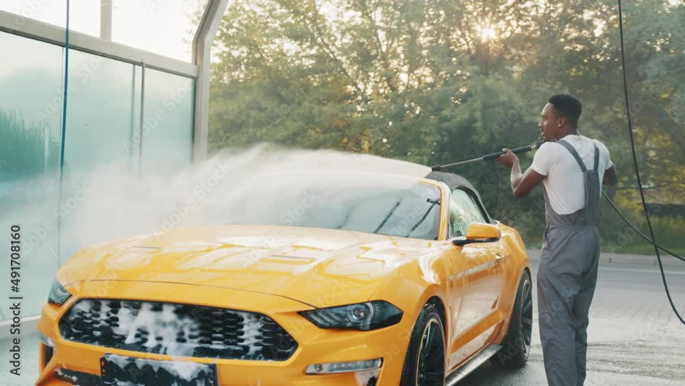 Manual car wash. Handsome African young man washing his luxury yellow ...