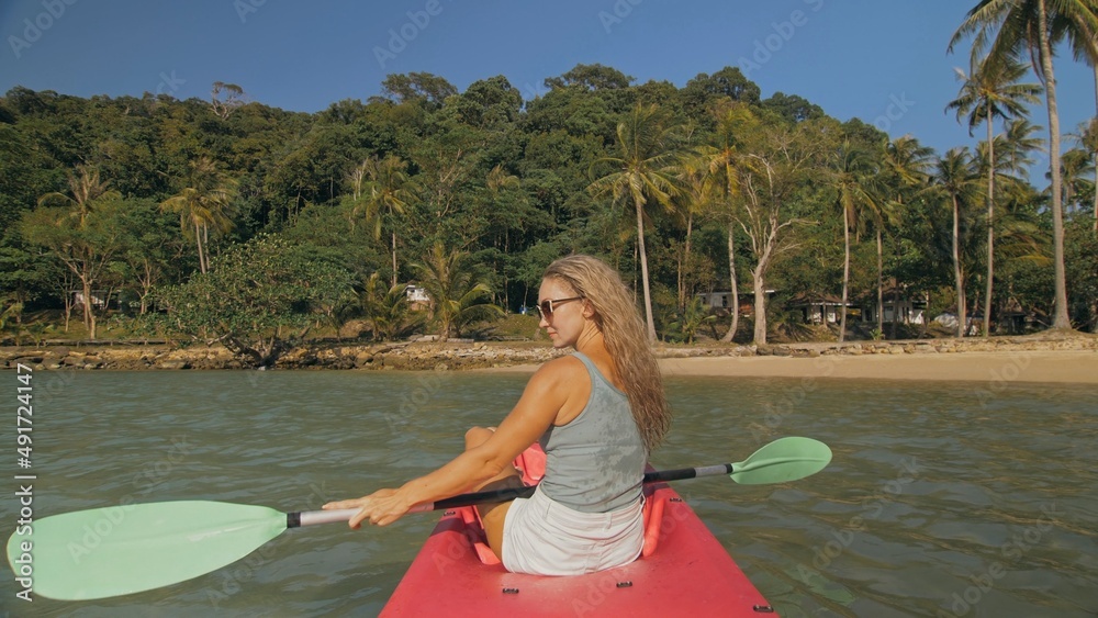 Long haired blonde woman with sunglasses rows bright pink canoe along ...