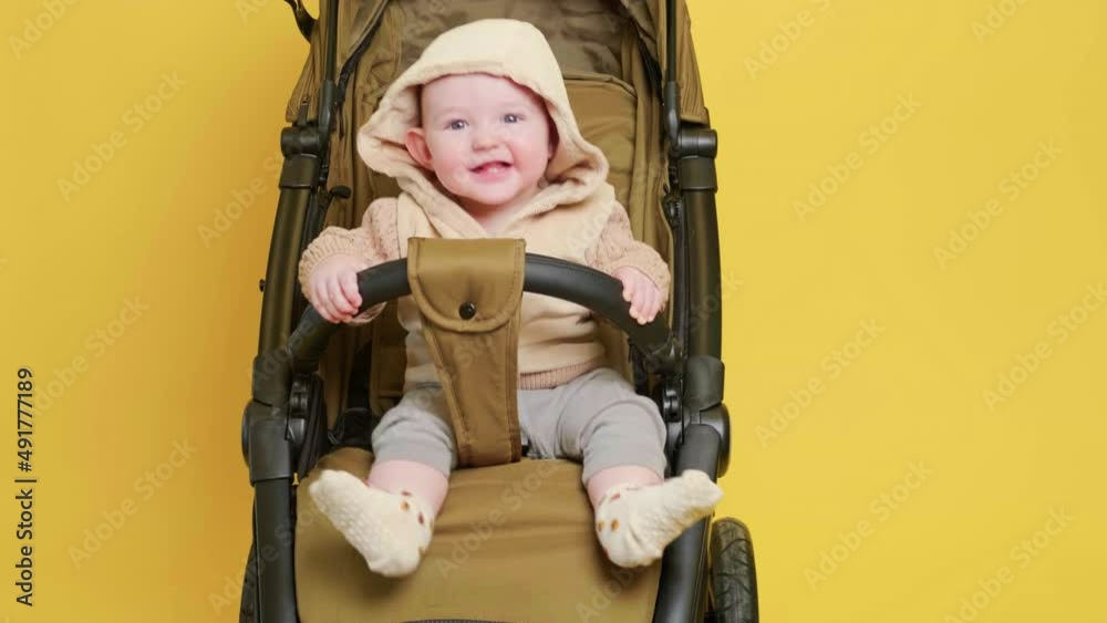 A happy child is sitting in a baby carriage on a studio yellow ...