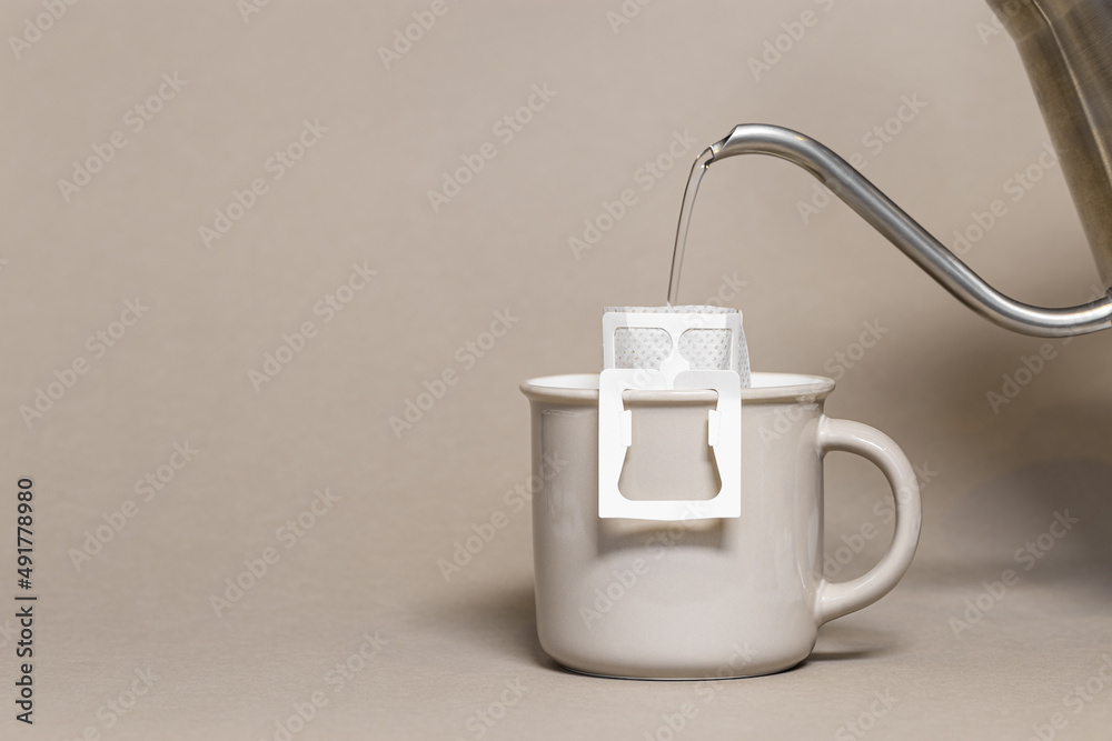 Drip coffee bag with ground coffee in big cup, hot water is poured into ...