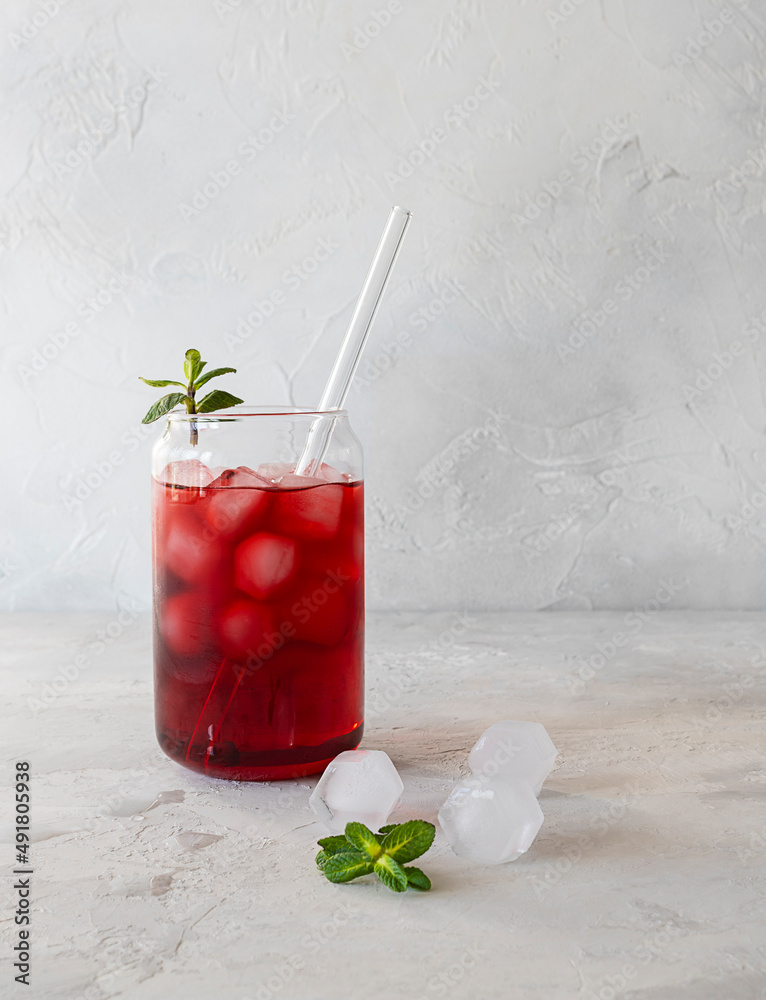 Red iced tea with a transparent glass with a straw on a light table ...