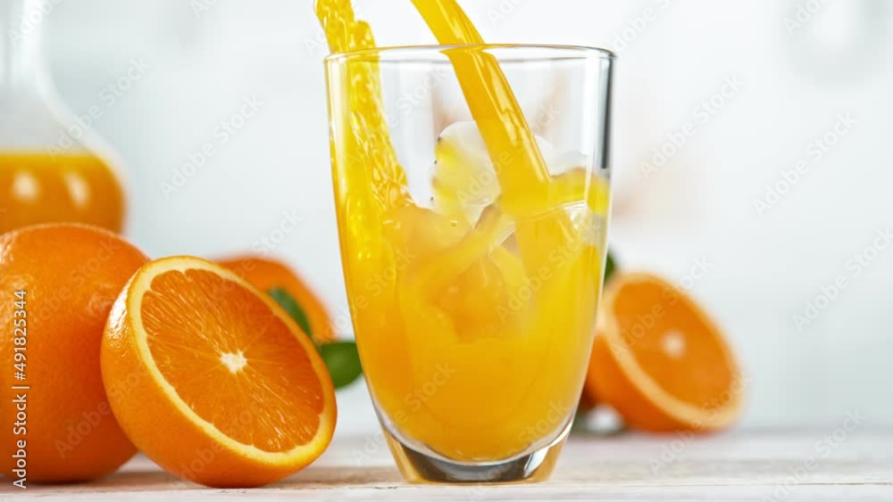 Super slow motion of pouring orange juice into glass. Placed on white ...