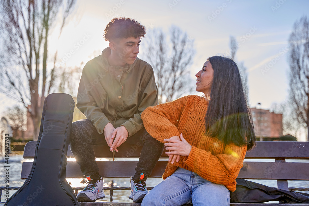 Two happy friends are talking and laughing while sitting on an outdoor ...