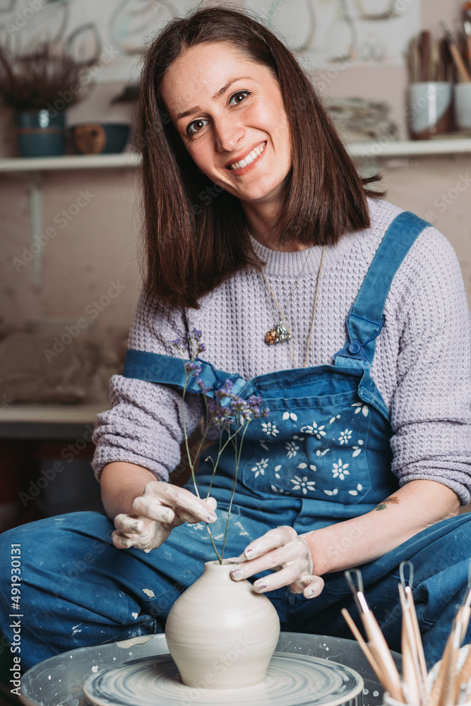 Smiling female potter working on pottery wheel while sitting in her ...