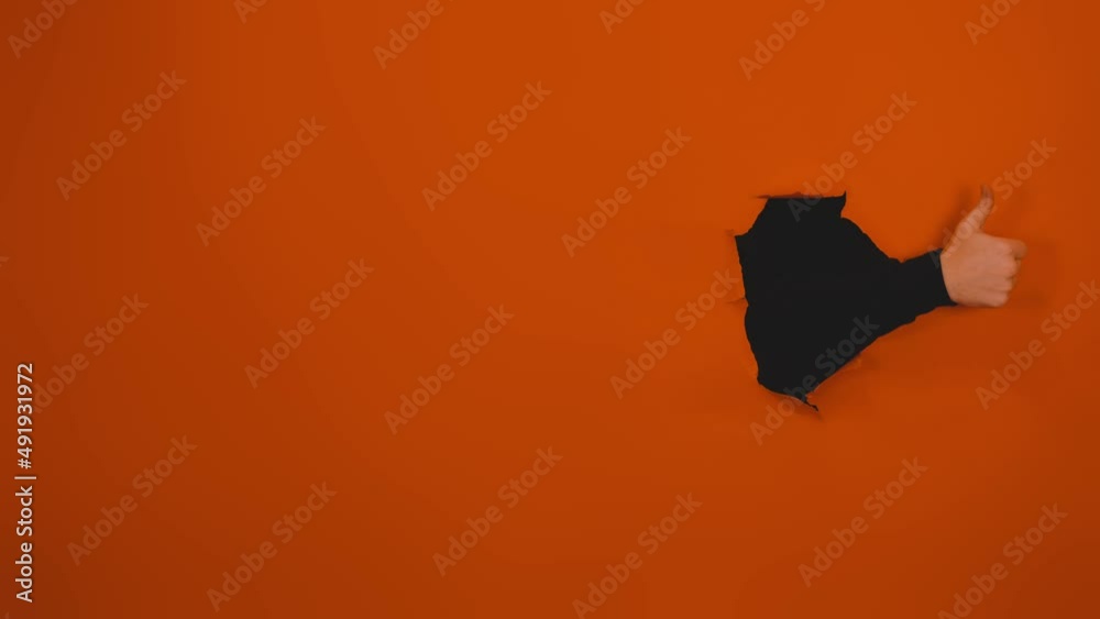 Man's hand showing thumb up and sticking out of hole of orange ...