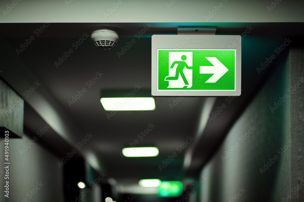 Green fire exit sign on hallway aside of smoke alarm device. Fire ...
