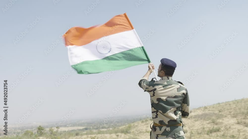 Back view shot of Indian soldier holding waving Indian flag on top of ...