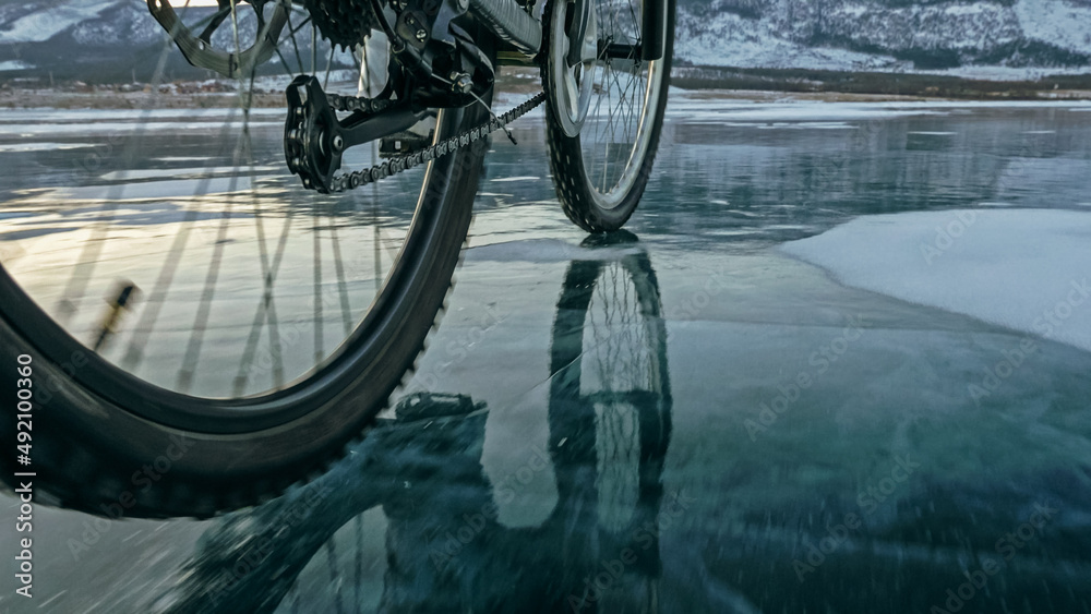 Woman is riding bicycle on the ice. Girl is dressed in a silvery down ...