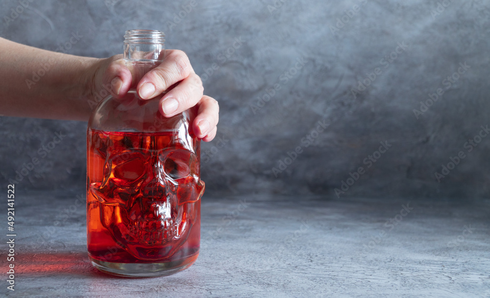 flacon with red liquid in a woman's hand on a dark background. bottle ...
