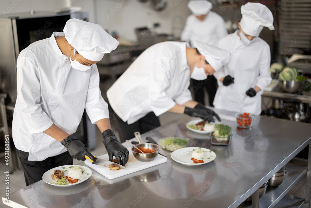 Multiracial group of cooks finishing main courses while working ...