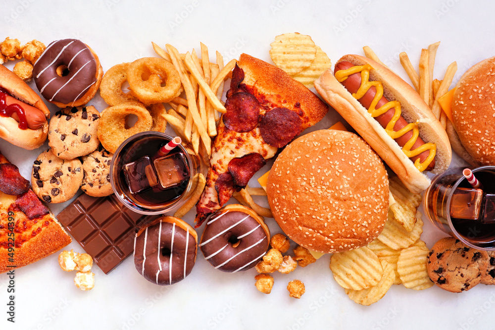 Junk food table scene scattered over a white marble background ...