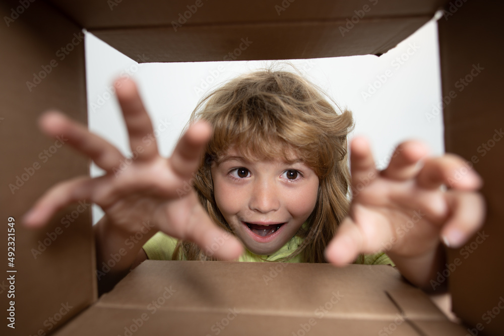 Funny excited child unpacking and opening the carton box looking inside ...