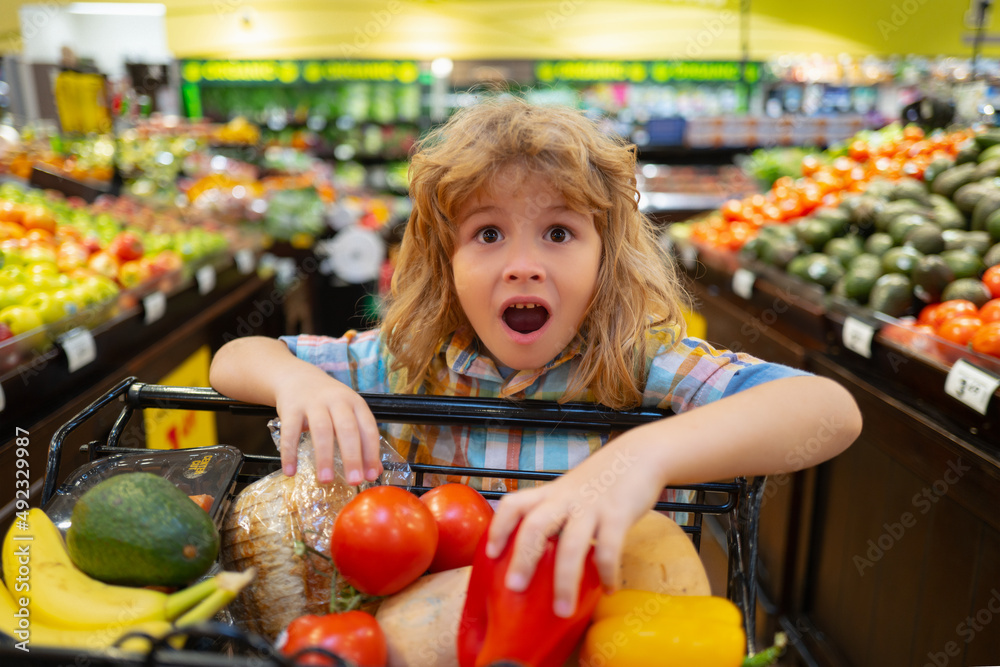 Child in the supermarket. Funny excited little boy wit shopping cart ...