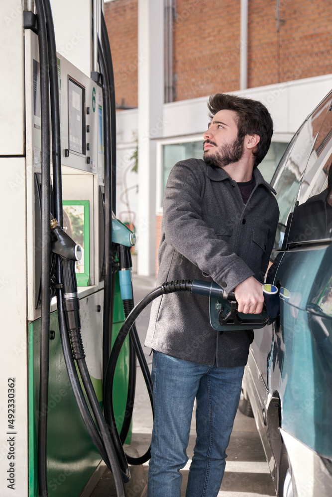 Young man refueling his vehicle with gasoline while looking at the ...