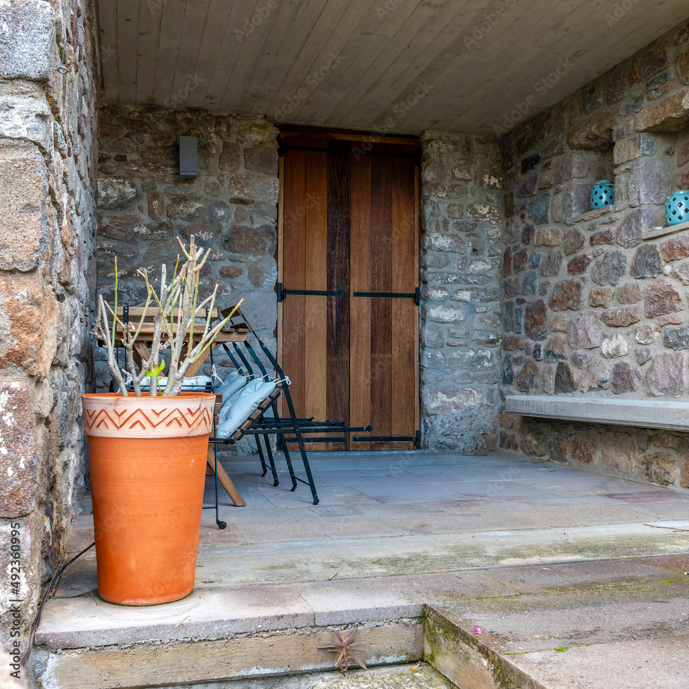 A stone house entrance with a wooden door, a potted plant, chairs and a ...
