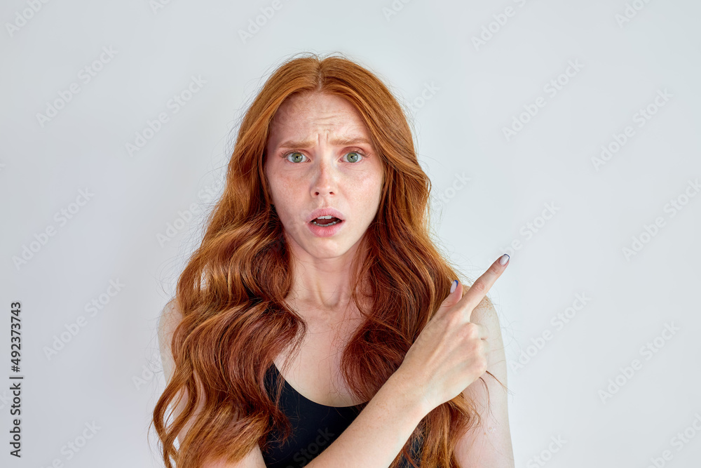 Confused redhead female showing at side pointing finger up at copy ...