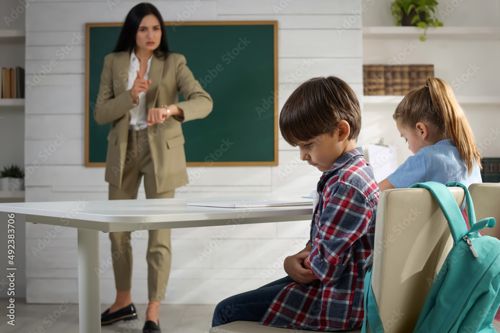 Teacher pointing on wrist watch while scolding pupils for being late in ...