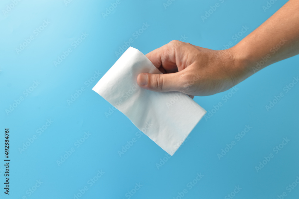 Hand holding white paper tissue isolated on a blue background. Hygiene ...