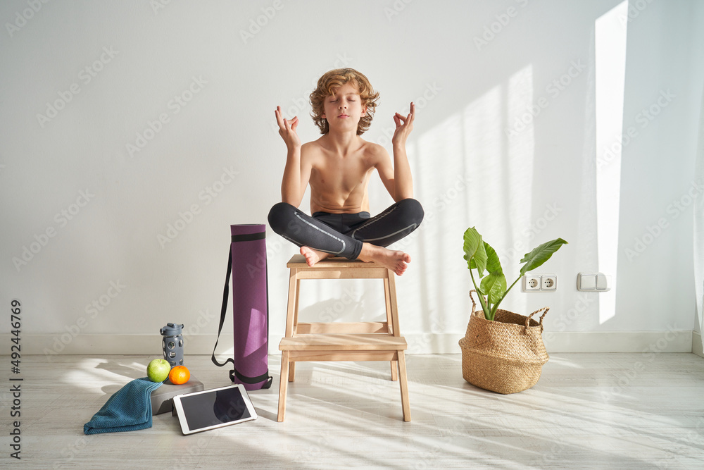 Preteen boy meditating in Lotus pose sitting on stool Stock Photo ...