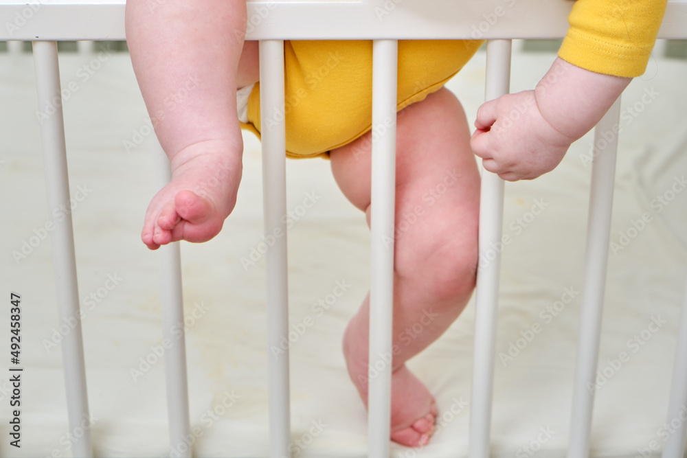 Toddler baby climbs the crib railing, legs close-up. Protect children ...