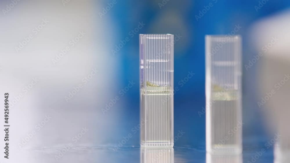 Two chemical cuvettes with a yellow liquid on a glass table, a yellow ...