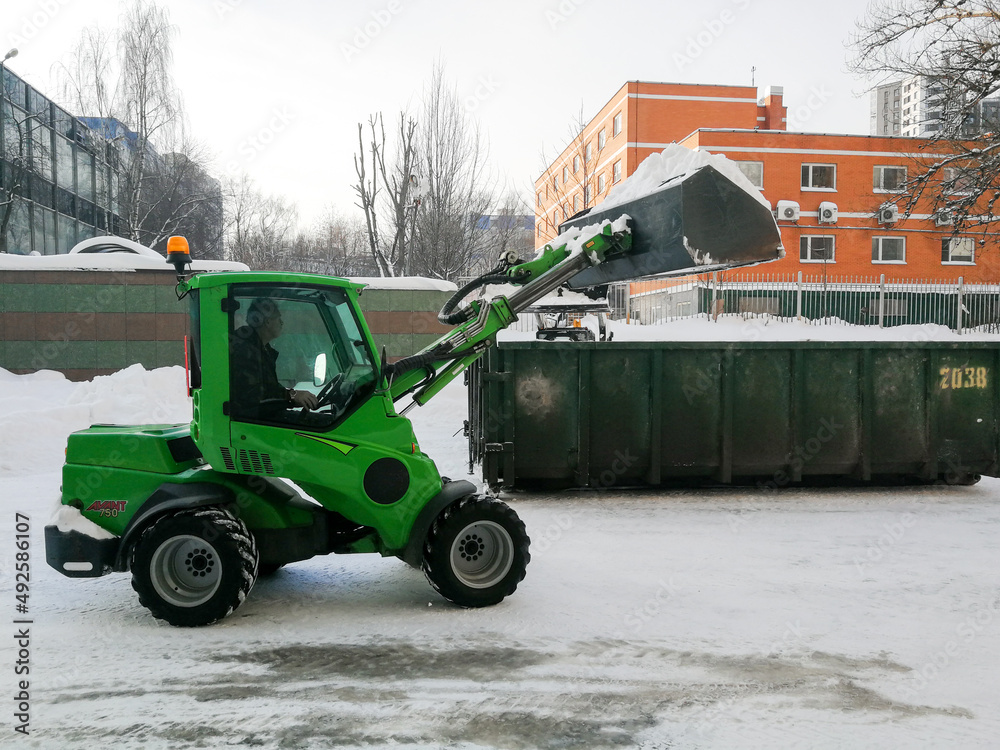Small front-end loaders clear snow from the street and load into a ...