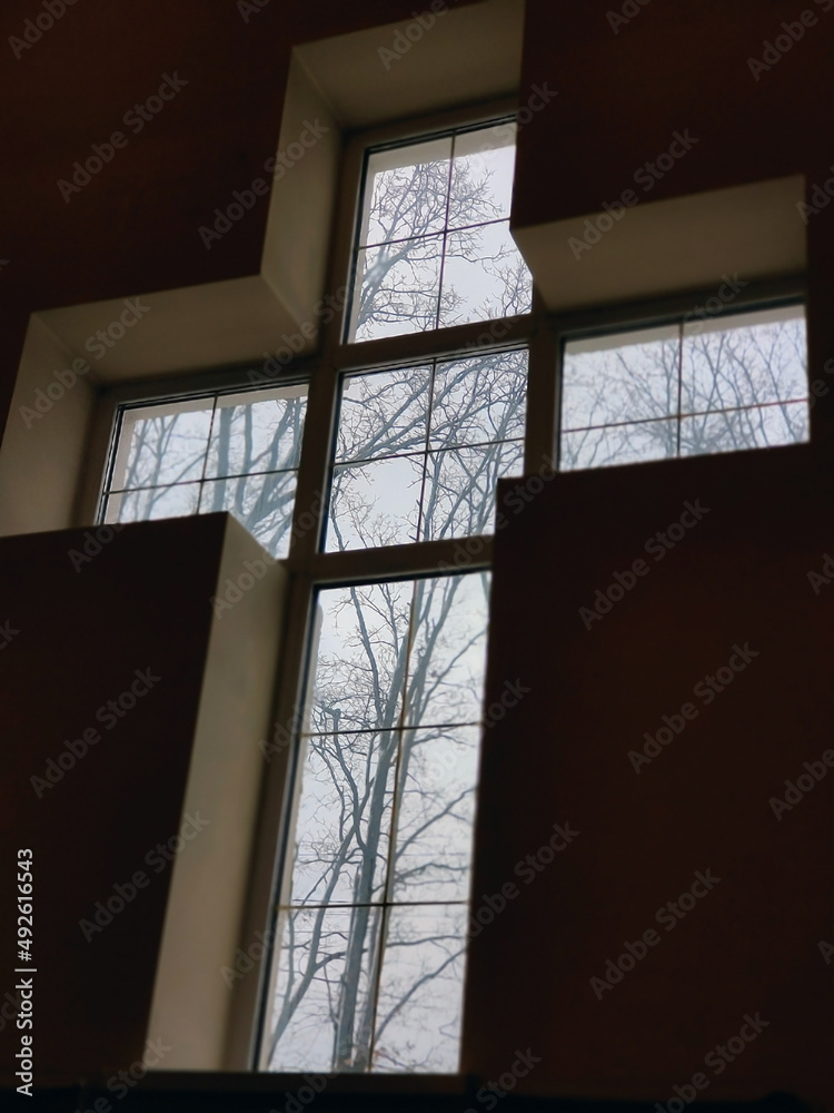 The window in the church is in the shape of a cross. Outside the window ...